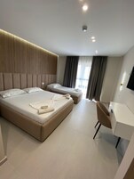 Quarto de hotel moderno com uma cama grande, uma cama menor, uma escrivaninha e uma cadeira.