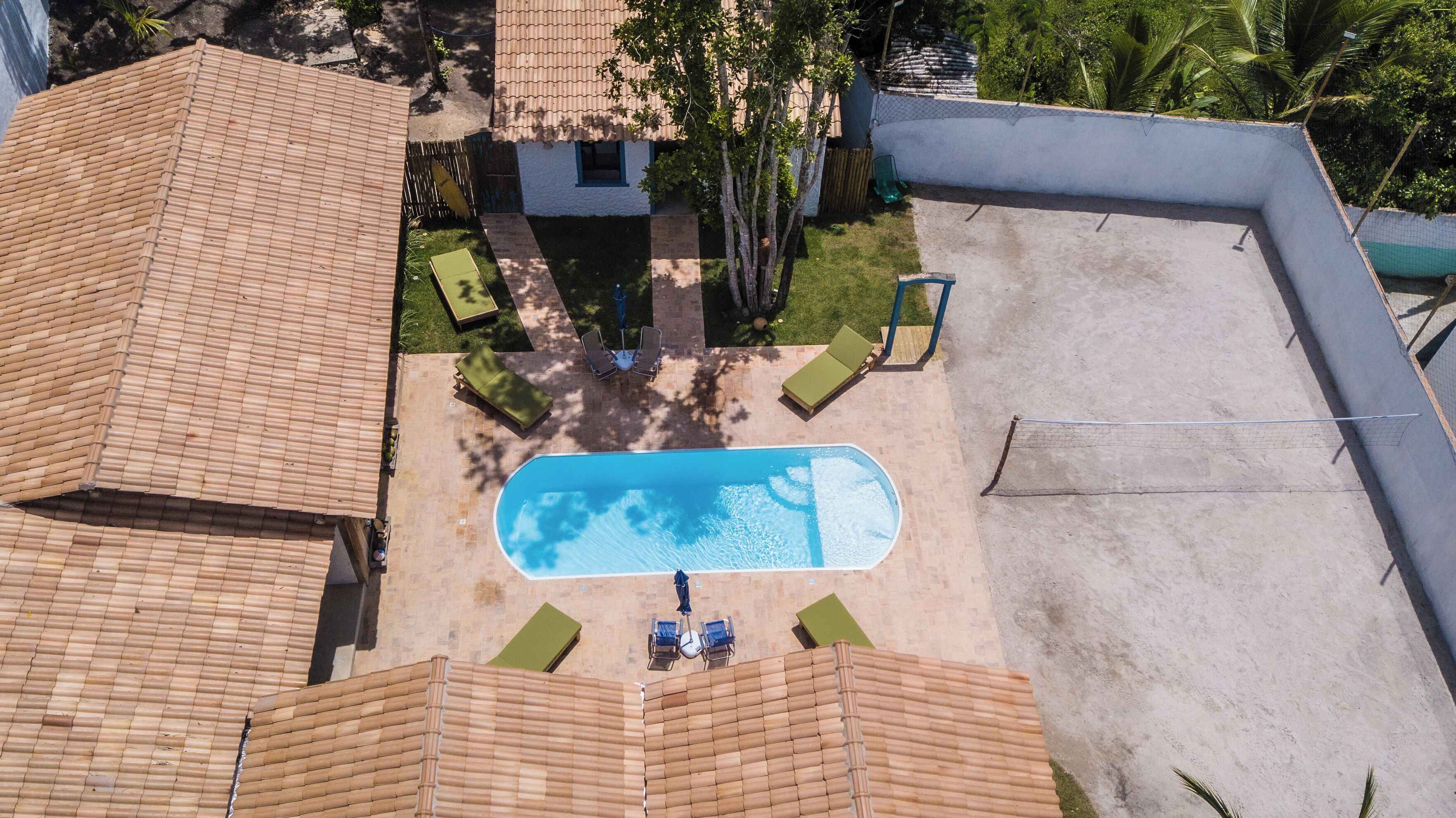 Vista aérea de um bairro residencial com piscina, cadeiras de descanso e um quintal cercado.