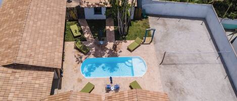 Vista aérea de um bairro residencial com piscina, cadeiras de descanso e um quintal cercado.