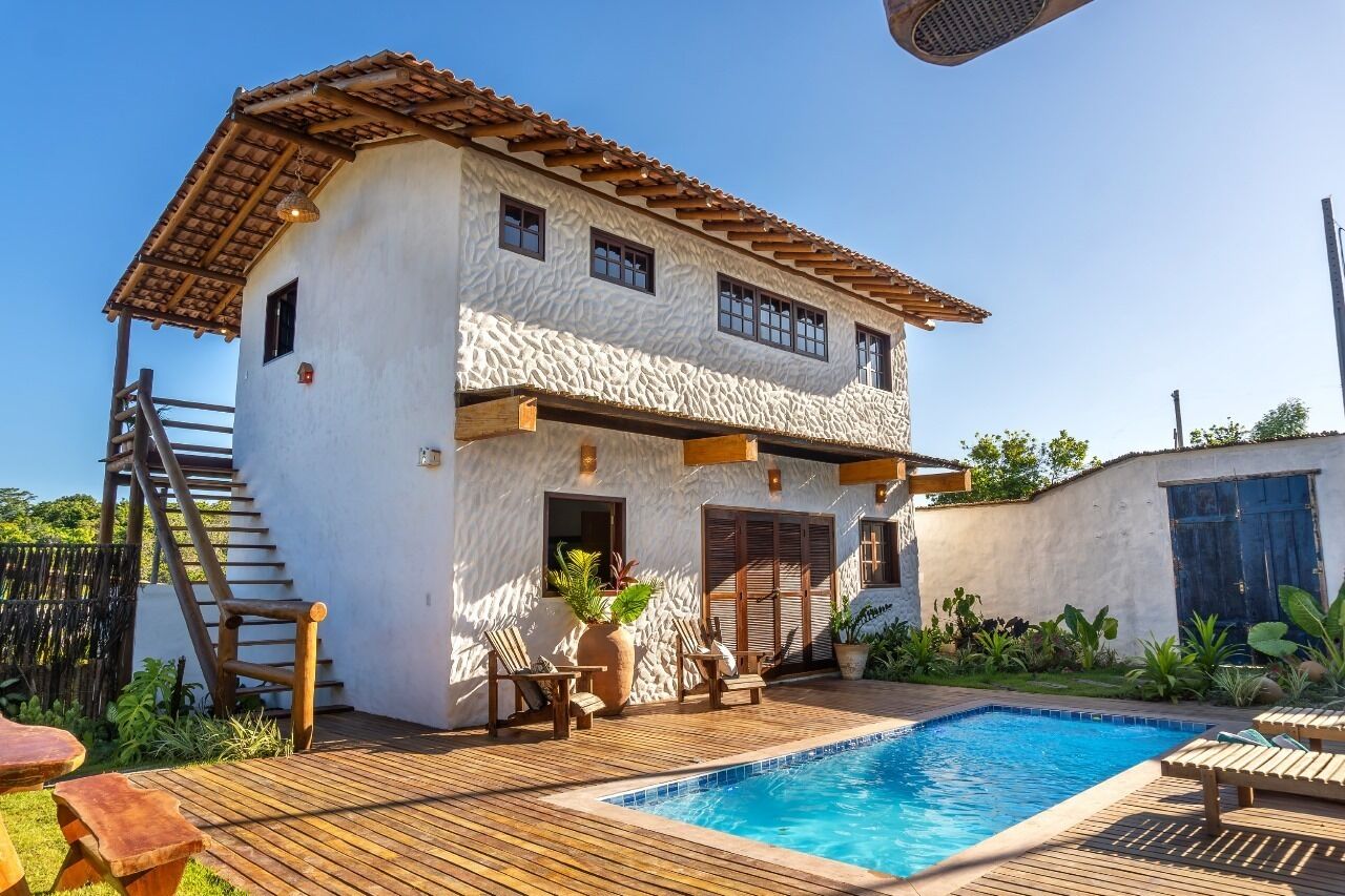 Uma casa de dois andares com piscina, deck de madeira e área de estar ao ar livre.