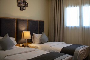 Quarto de hotel com duas camas, cabeceira, luminária e janela com cortinas.