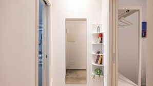 Um corredor com uma porta branca, um espelho e uma estante branca com livros e uma pequena planta.