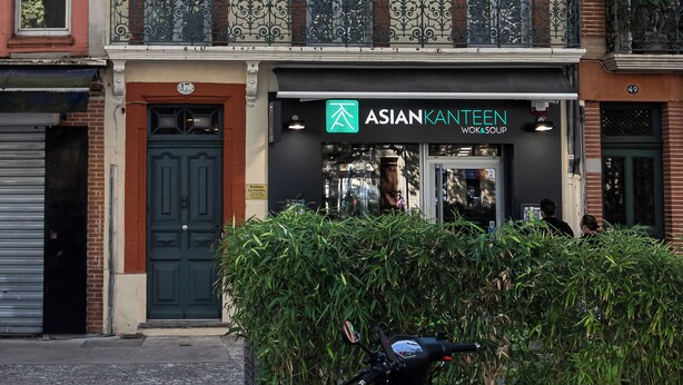 Um edifício de vários andares com um restaurante chamado "Asian Kanteen Wok & Soup" no andar térreo.