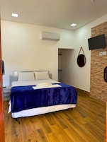 Quarto de hotel moderno com uma cama grande, piso de madeira, TV montada e ar condicionado.