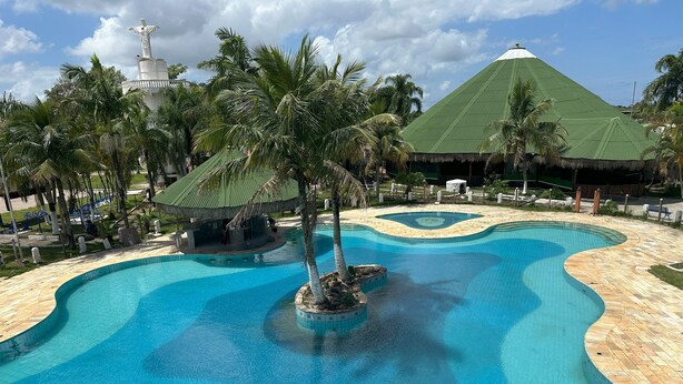 Piscina com tema tropical, cercada por palmeiras e uma estrutura com telhado de palha.