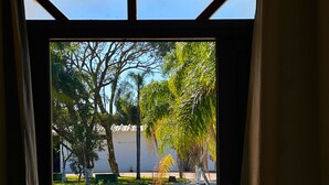 Vista pela janela, com calçada de tijolos, árvores e um edifício ao fundo.