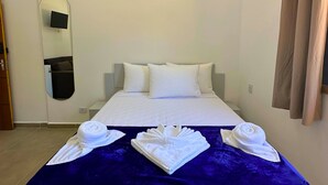 Quarto de hotel com uma cama grande, televisão de tela plana na parede e banheiro visível através de uma porta.