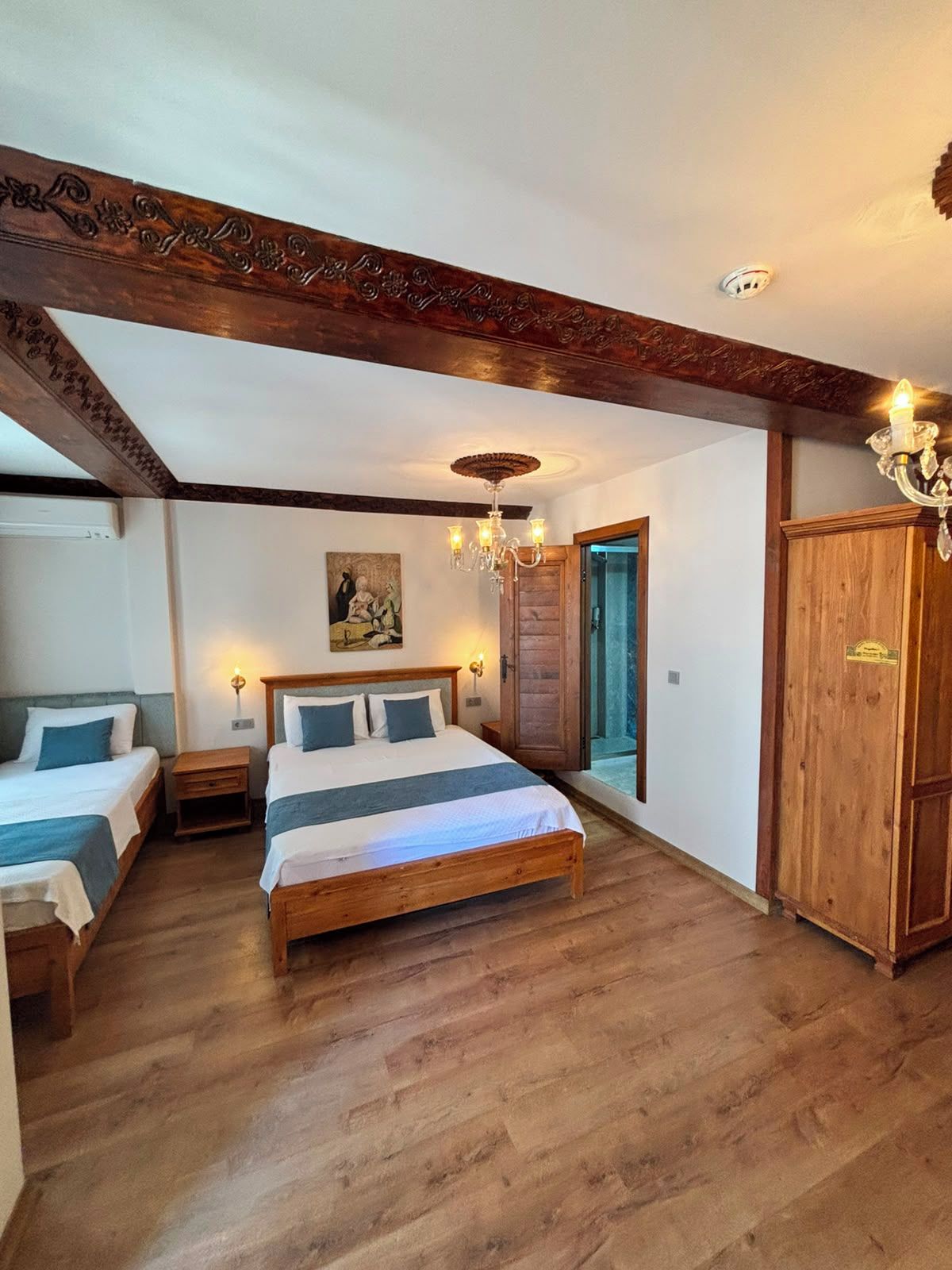 Quarto com duas camas, guarda-roupa de madeira, um candelabro e um quadro na parede.