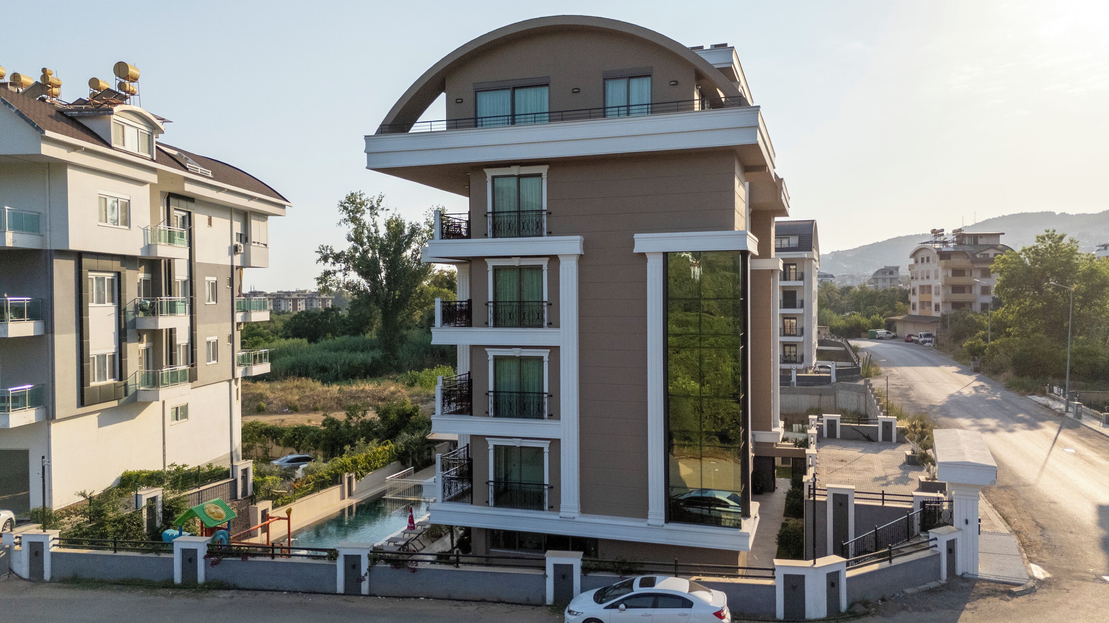 Um edifício moderno de vários andares com varandas, piscina e vista para uma área residencial.