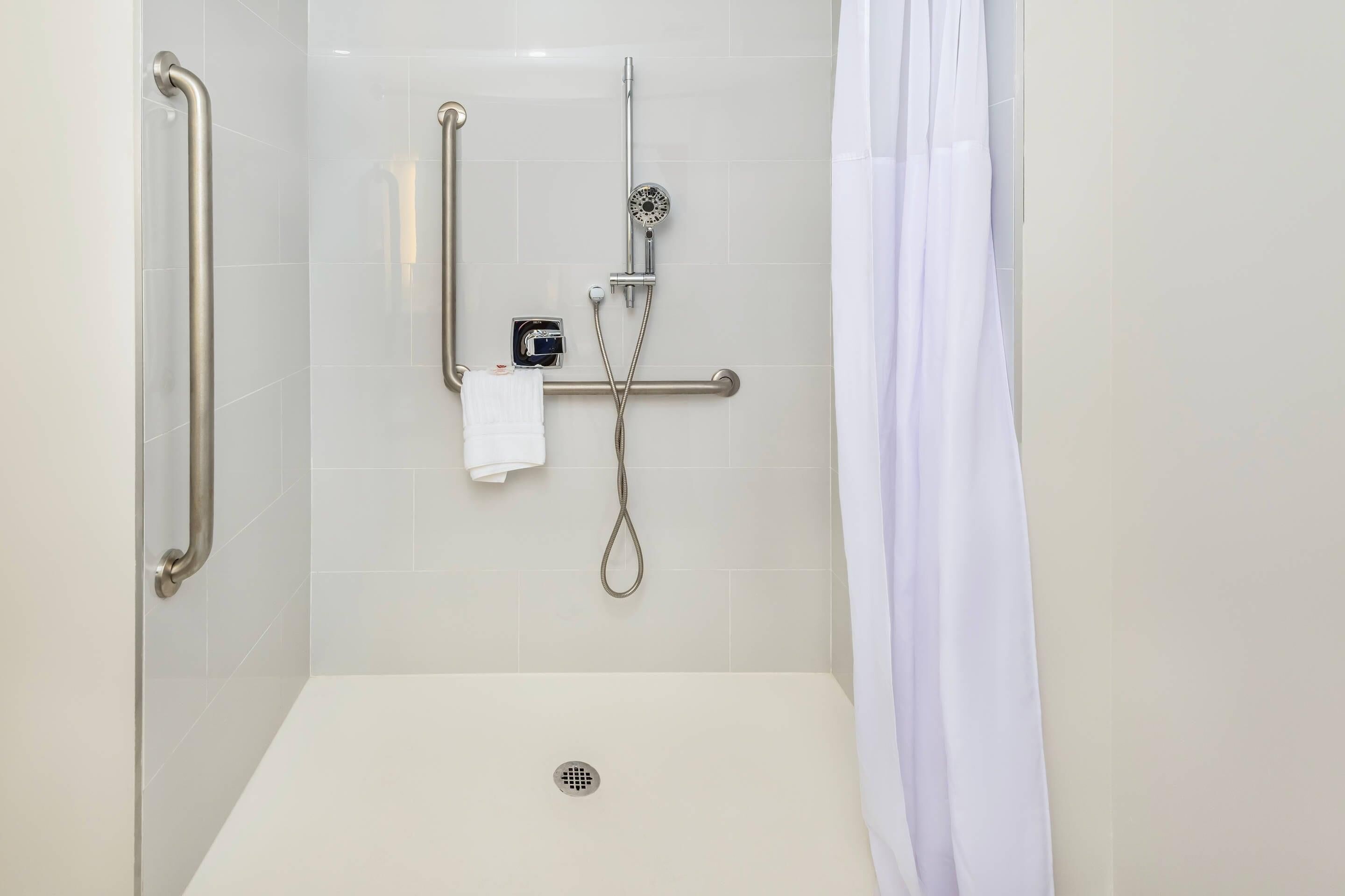 Área de chuveiro com barra de apoio, chuveiro manual e porta-toalhas.