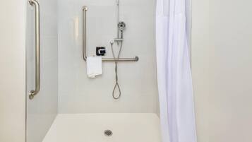 Área de chuveiro com barra de apoio, chuveiro manual e porta-toalhas.