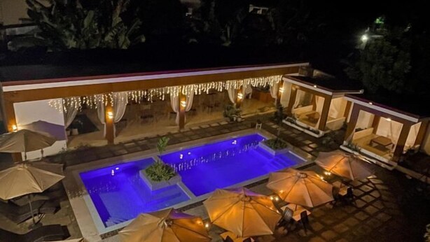 Uma área de piscina com guarda-sóis e cadeiras, rodeada por um deque coberto com luzes de corda.