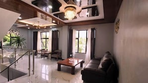 Uma sala de estar ampla com piso de mármore, sofá de couro, mesa de centro de madeira e um candelabro.