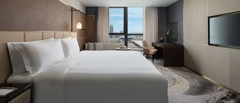 Quarto de hotel com uma cama grande, uma escrivaninha, uma cadeira, uma televisão e vista para a paisagem urbana.