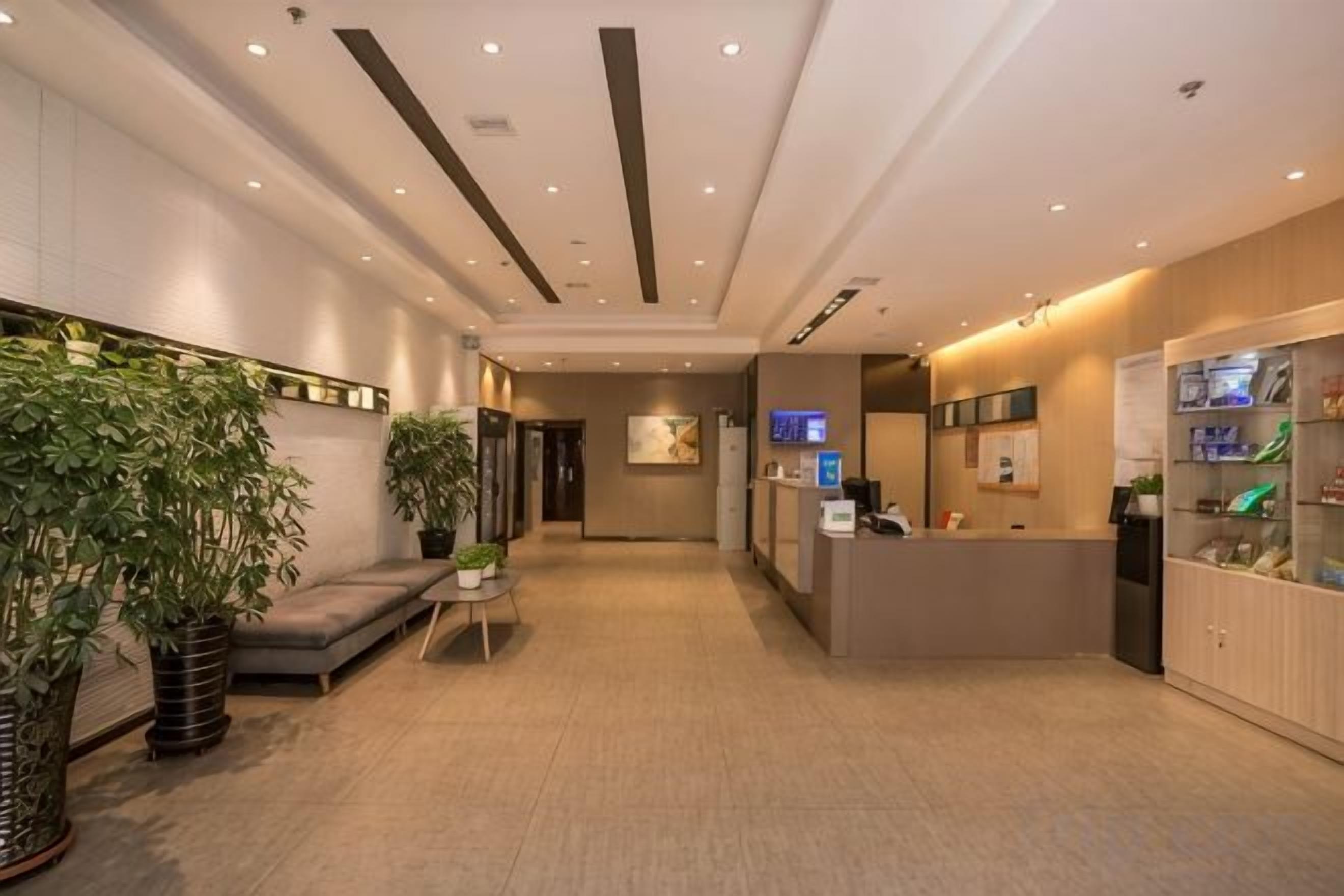 Um hall de hotel com balcão de recepção, área de estar e plantas em vasos.