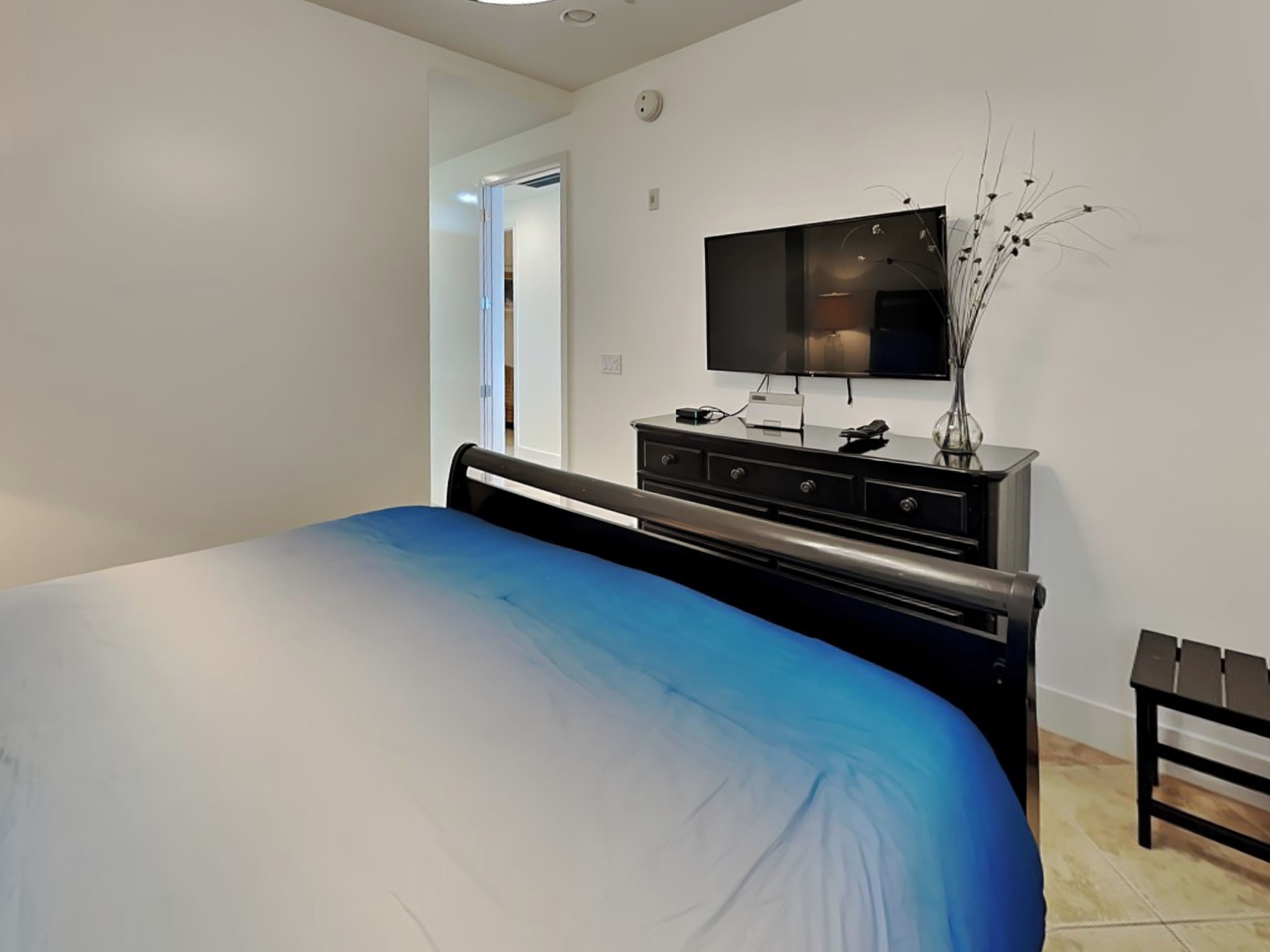 Um quarto com uma cama, penteadeira, televisão e um banquinho.
