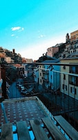 Vista de uma varanda com vista para um horizonte urbano, edifícios, uma rua estreita e uma torre ao longe.