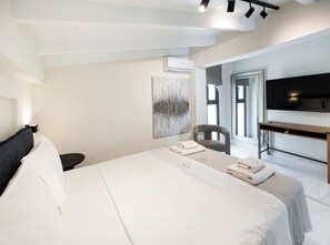 Quarto de hotel moderno com uma cama grande, uma mesa de escritório, uma cadeira e uma televisão.