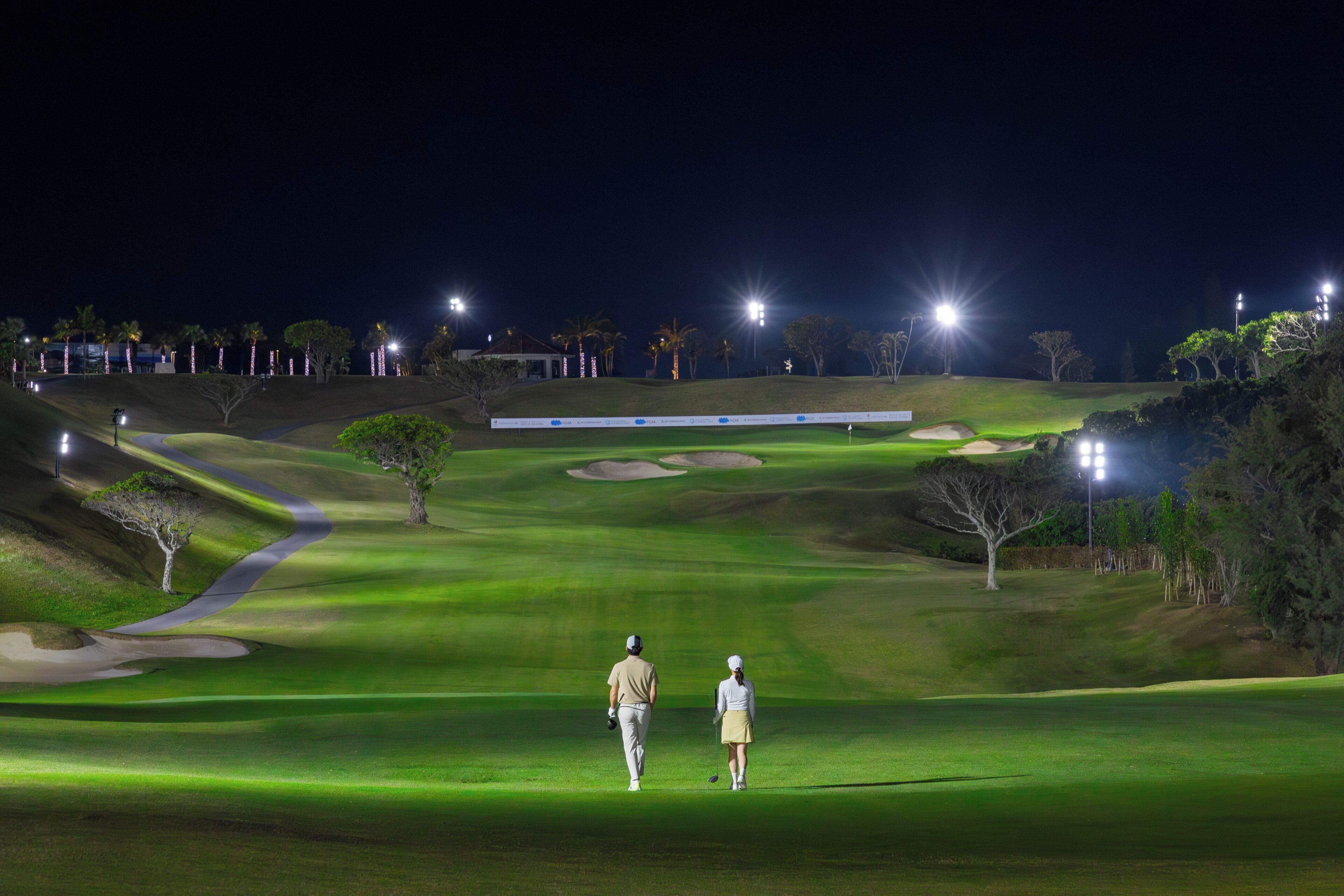 Um campo de golfe à noite com iluminação, um gramado bem cuidado e um caminho claro.