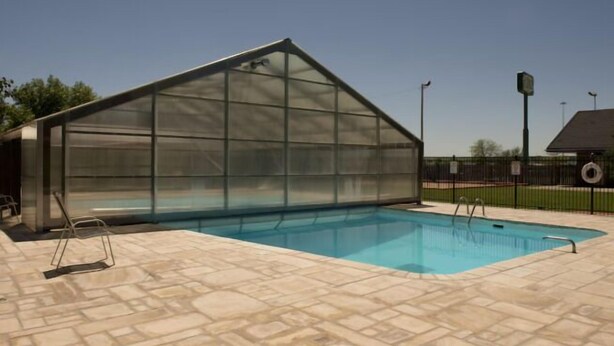 Piscina com área envidraçada, possivelmente uma estufa, e um deck revestido com azulejos.