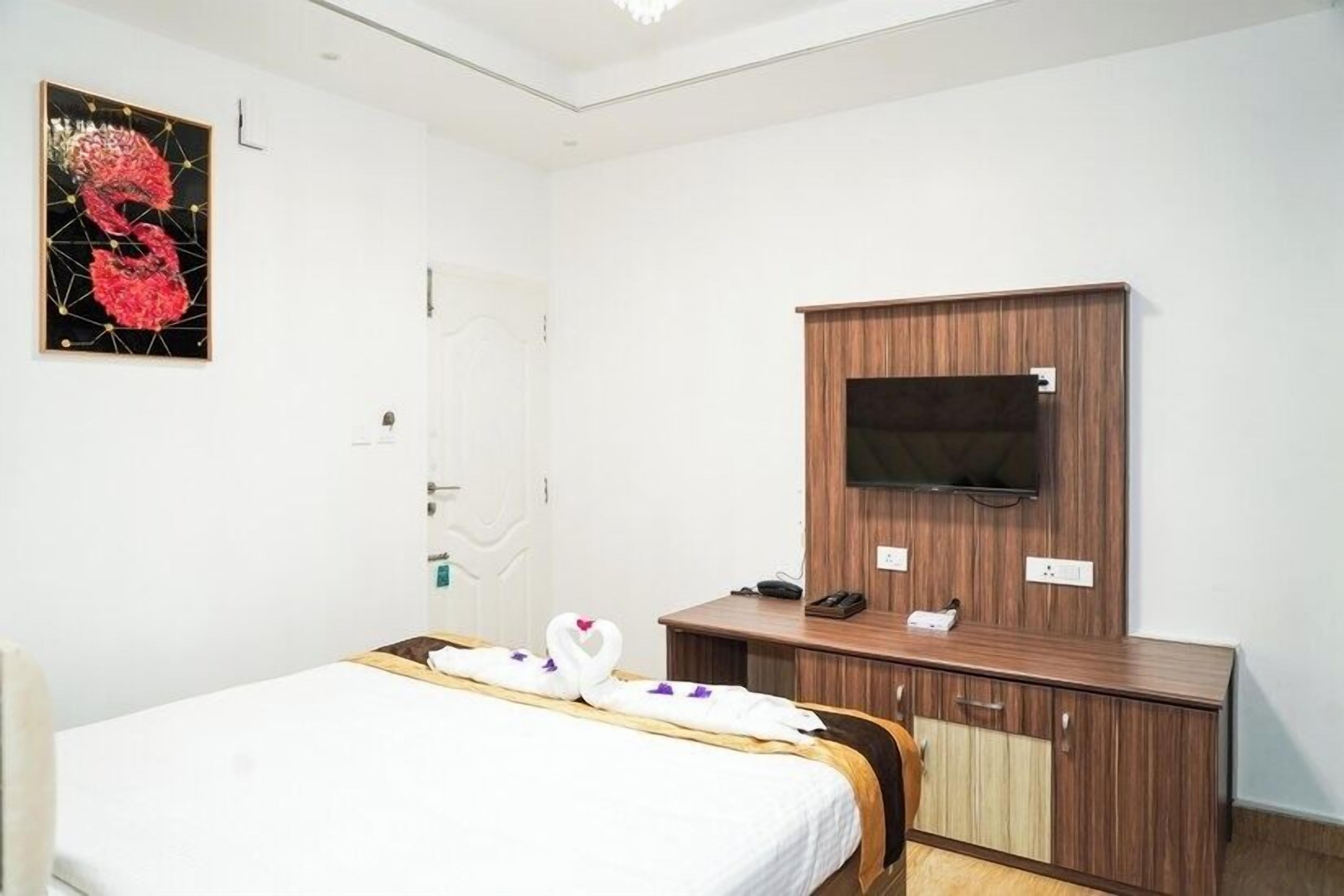 Quarto de hotel com cama, guarda-roupa de madeira e televisão, além de uma obra de arte na parede.