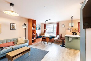 Uma sala de estar moderna com sofá, mesa de centro e área de jantar com cadeiras e mesa. Há uma estante, uma janela com cortinas, e uma cozinha com bancada e pia.