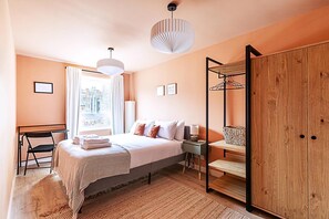 Quarto com cama, mesa de cabeceira, abajur, guarda-roupa e vista para a cidade.