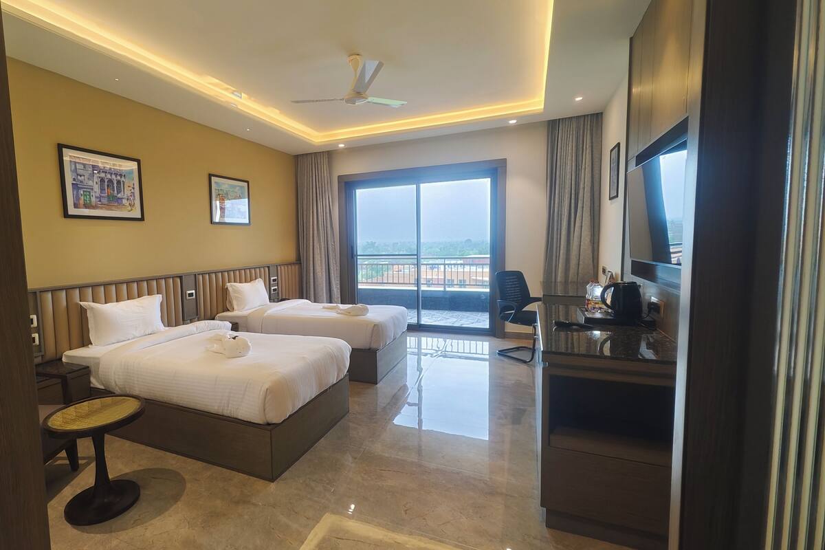Quarto de hotel com duas camas, uma escrivaninha, uma cadeira, uma mesa pequena e varanda com vista.