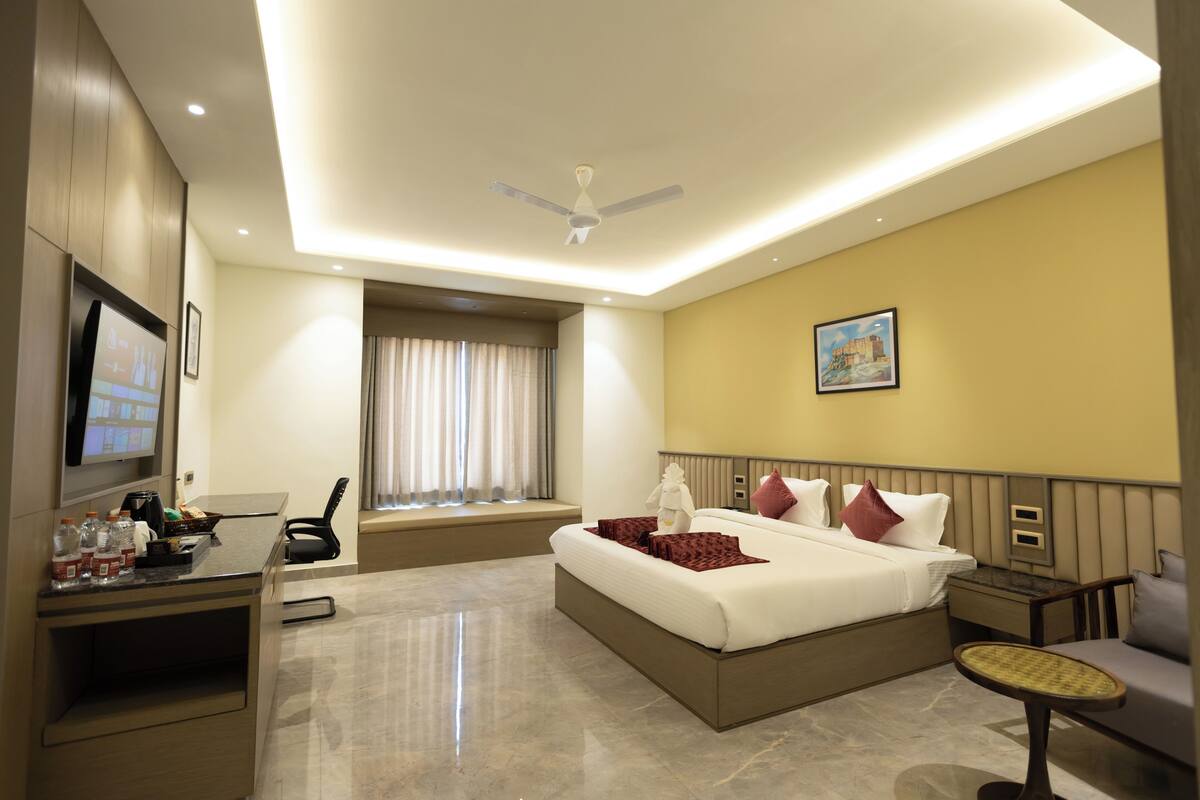 Quarto de hotel com cama, escrivaninha, cadeira e televisão.
