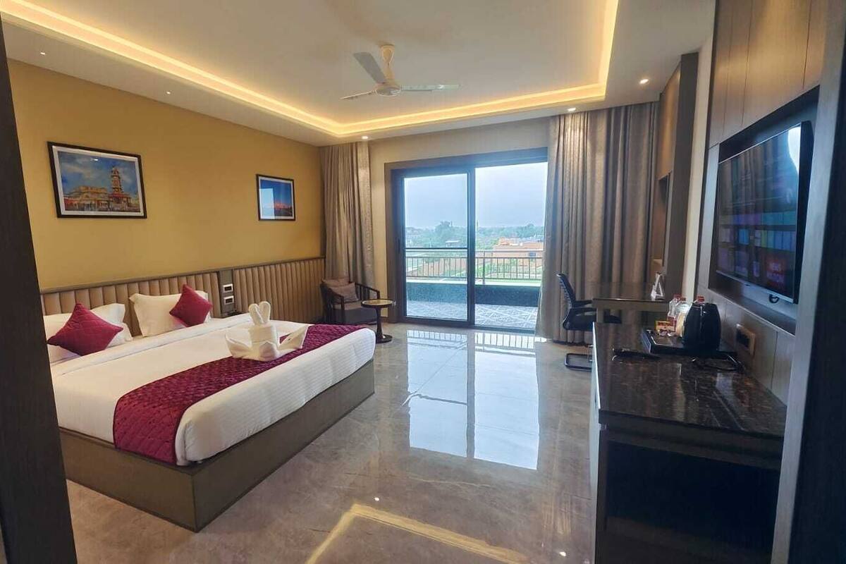 Quarto de hotel com cama grande, televisão de tela plana, varanda com vista e máquina de café.