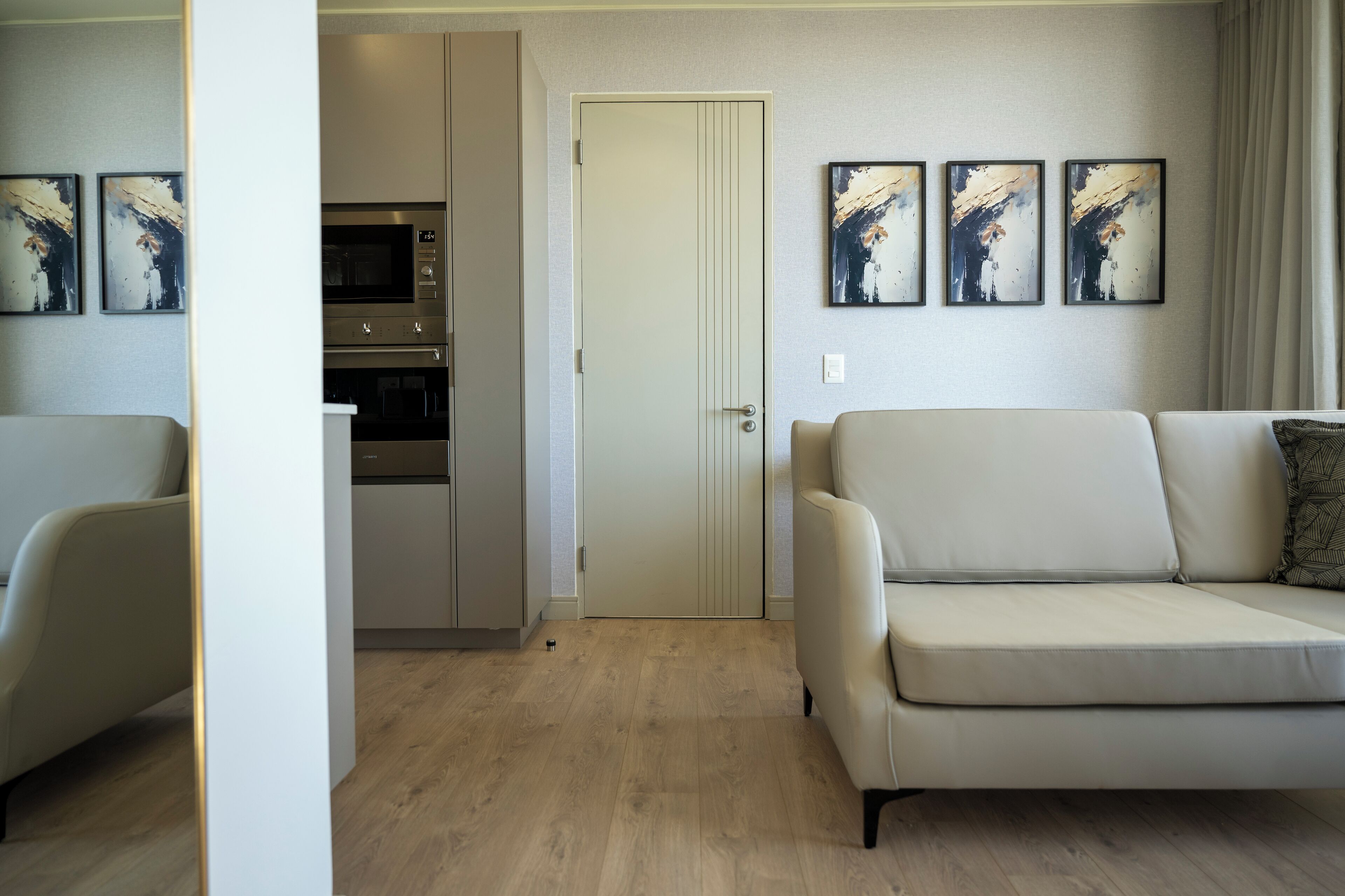 Uma sala moderna com um sofá bege, uma área de jantar com mesa e cadeiras, e uma cozinha com micro-ondas e forno.