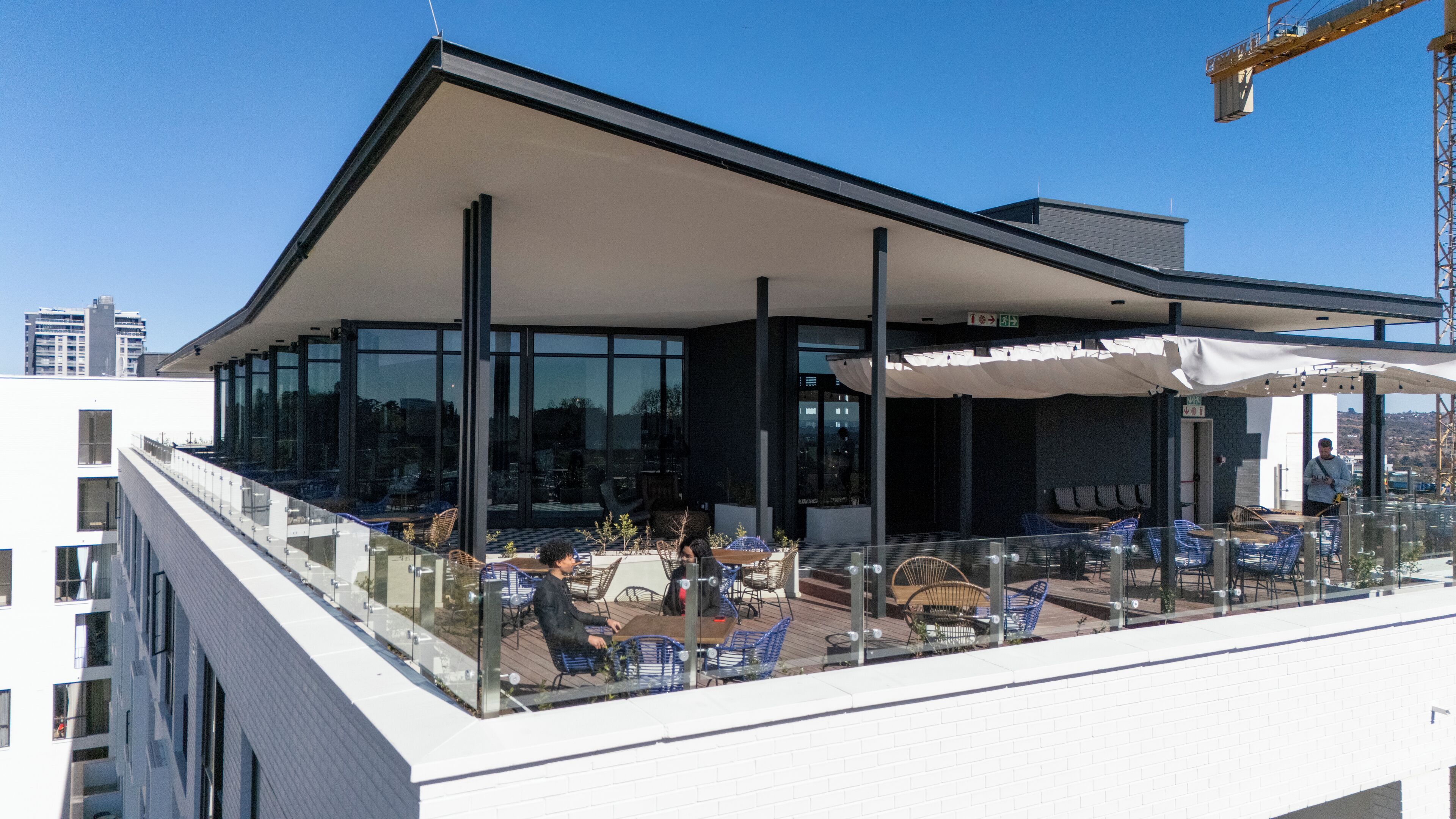 Uma área de estar moderna ao ar livre, com guarda-corpos de vidro e parte coberta.
