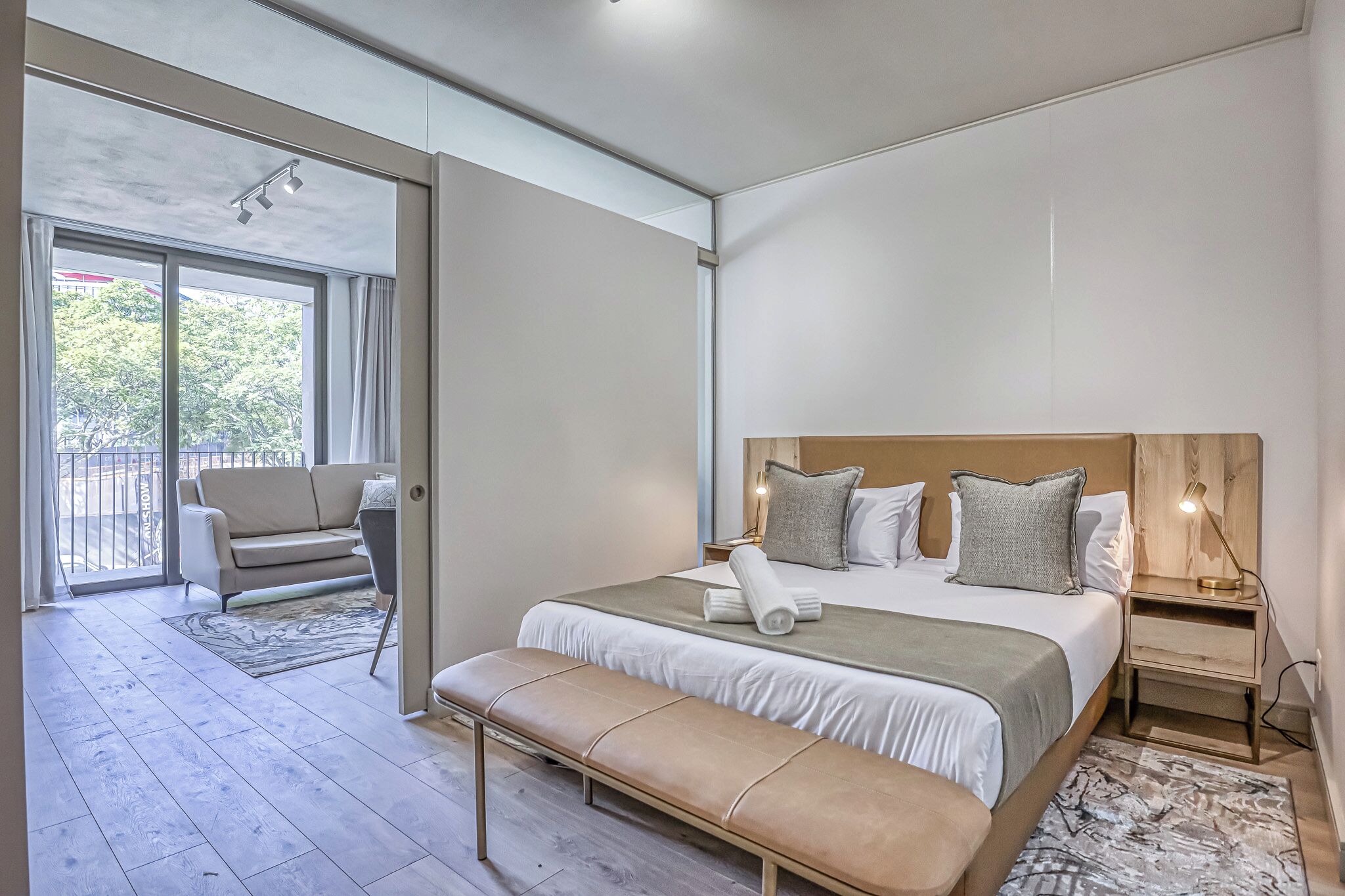 Quarto moderno com cama grande, um banquinho, uma mesa de cabeceira e uma cadeira.
