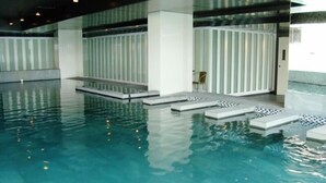 Piscina interior com água cristalina, degraus brancos que levam à piscina e um design arquitetônico moderno com linhas verticais nas paredes.