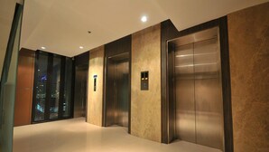 Área moderna de elevadores com três cabines, parede de vidro e piso polido.