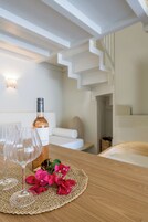 Uma mesa com uma garrafa de vinho, duas taças de vinho e flores cor-de-rosa sobre um jogo americano trançado.