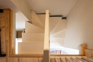 Escadaria com corrimão de madeira e vista para uma cama ao fundo.