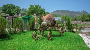 Tractor antigo com uma grande concha nas costas, rodeado por vegetação e um muro de pedra.