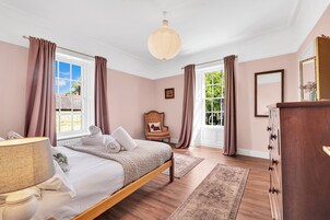 Um quarto com uma cama, cômoda, cadeira e uma janela grande com cortinas.