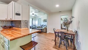 Cozinha com ilha de madeira, mesa de jantar com cadeiras e vista para a sala de estar.