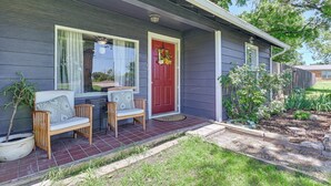 Uma casa com porta vermelha, varanda com duas cadeiras e um pequeno jardim.