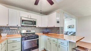 Cozinha com armários brancos, micro-ondas, fogão e painel de azulejos.