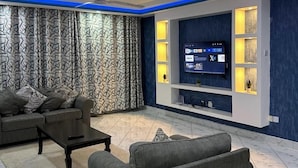 Uma sala de estar moderna com um sofá cinzento, uma mesa de centro e uma TV na parede.
