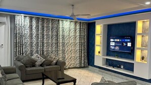 Uma sala de estar moderna com uma televisão de tela plana, sofás cinzas e cortinas estampadas.