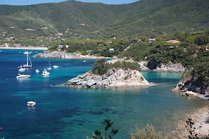 Paisagem costeira com águas turquesa cristalinas, afloramentos rochosos e alguns barcos.