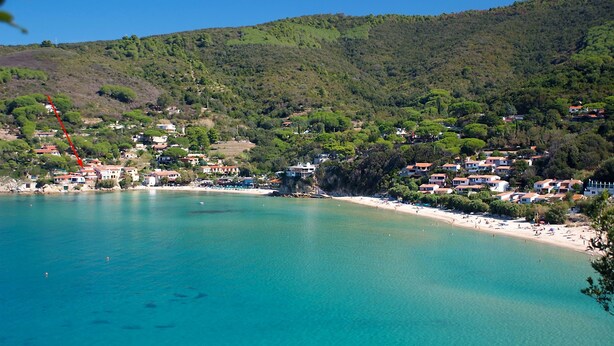 Uma vila costeira com praia, casas e um horizonte montanhoso.