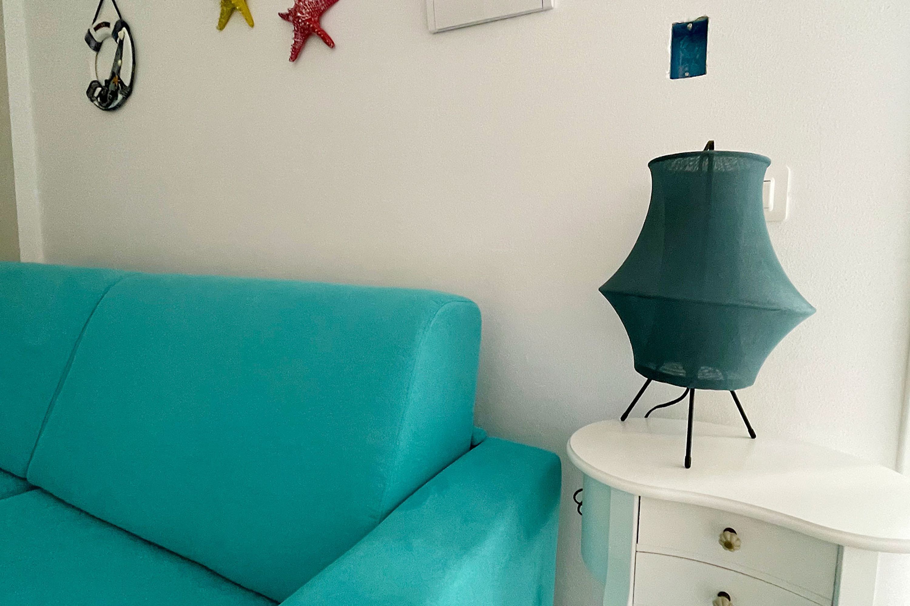 Um sofá verde-água e uma mesinha de cabeceira branca com uma luminária azul.