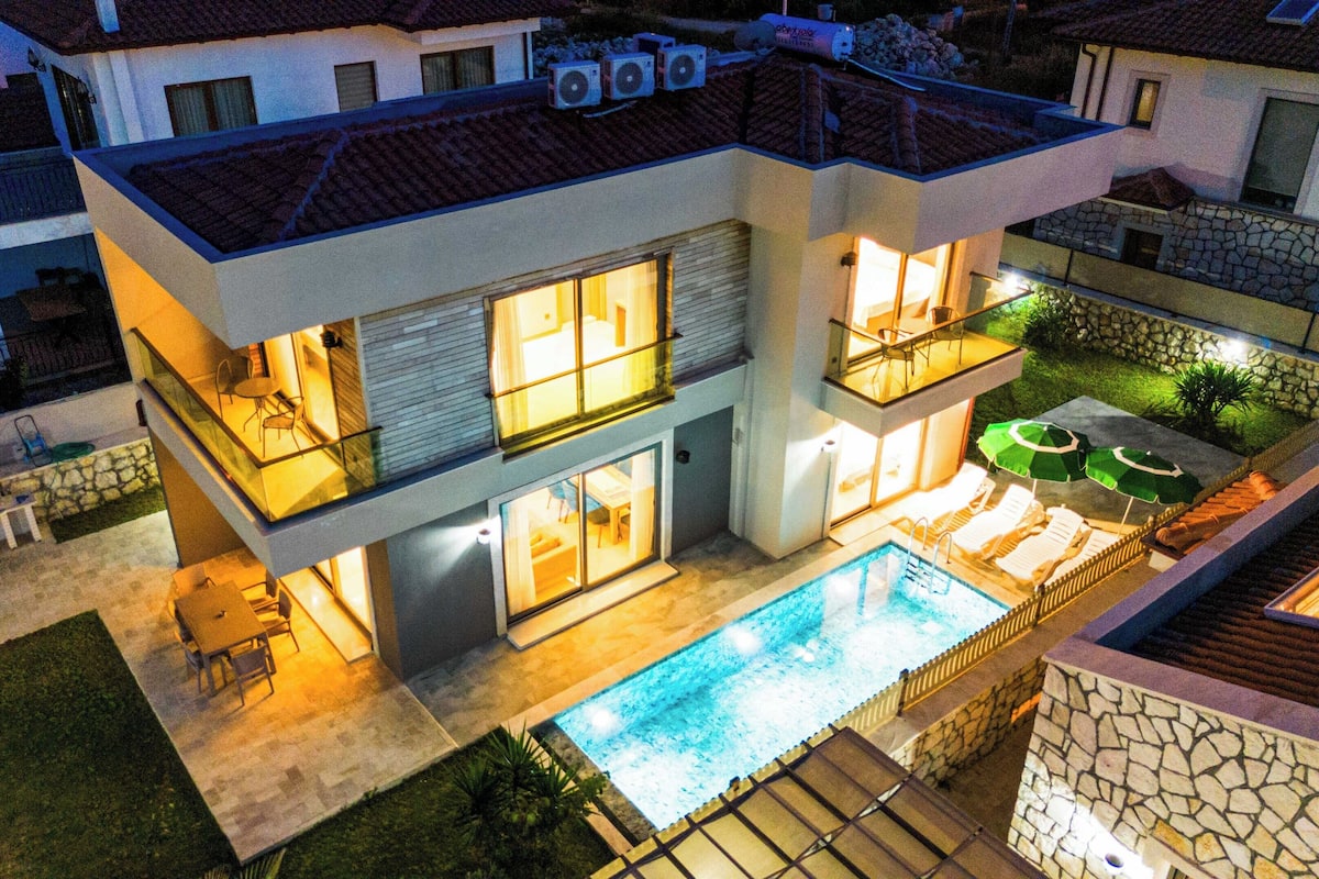 Uma casa moderna de dois andares com piscina, área de estar externa e muro de pedra.