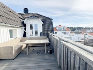 Um terraço com mobiliário de vime e uma mesa, com vista para uma área residencial com casas.