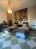 Quarto com duas camas, um lustre, um quadro grande e piso xadrez.